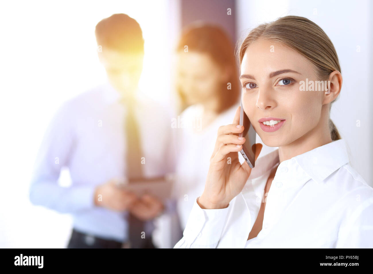 Serious blonde businesswoman talking by phone in the background of her ...