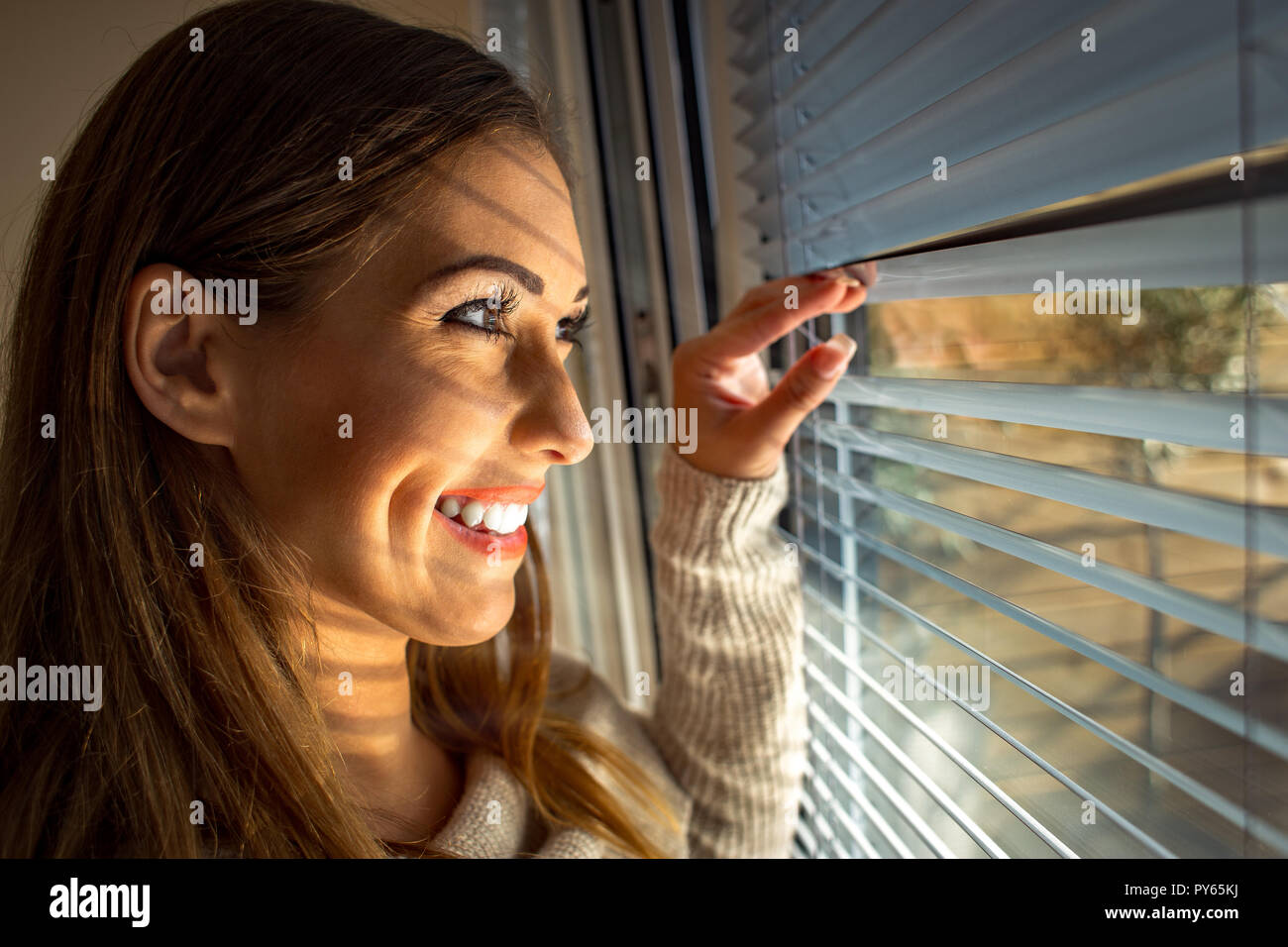 Beautiful woman looking through window and venetian blinds while ...