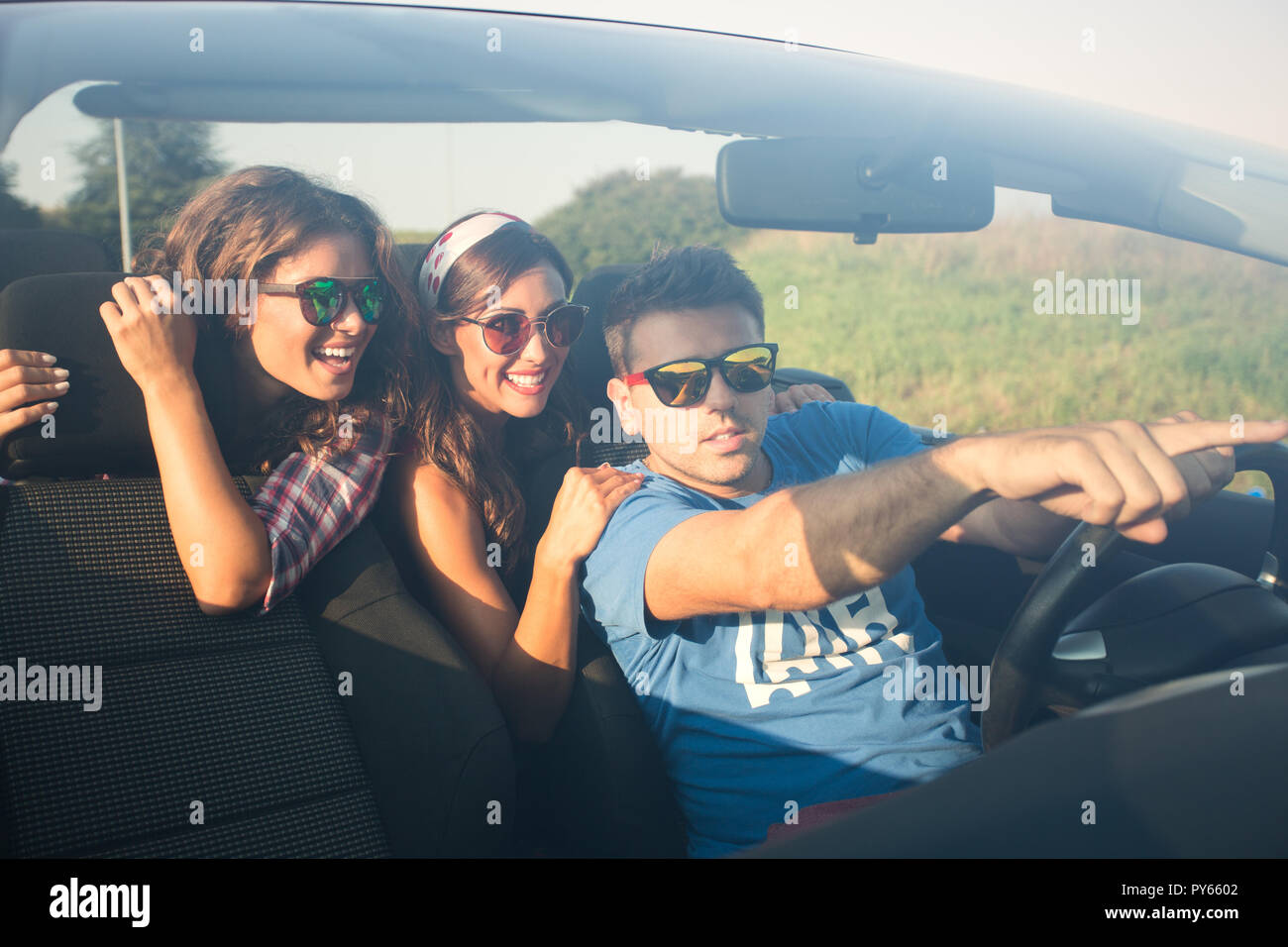 Three friends driving around in a convertible exploring pointing at ...