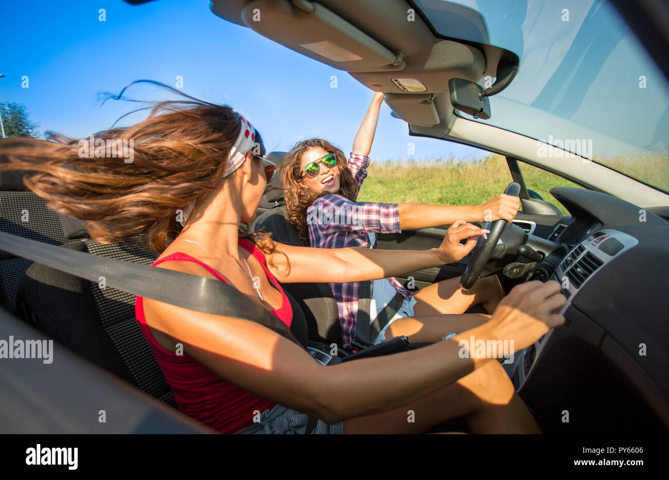 Two young beautiful girls driving in a convertible while dancing in ...