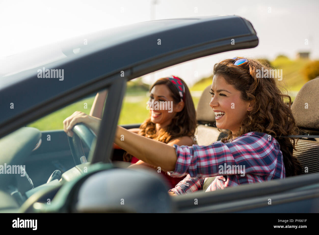 Two young beautiful girls driving in a convertible while smiling Stock ...