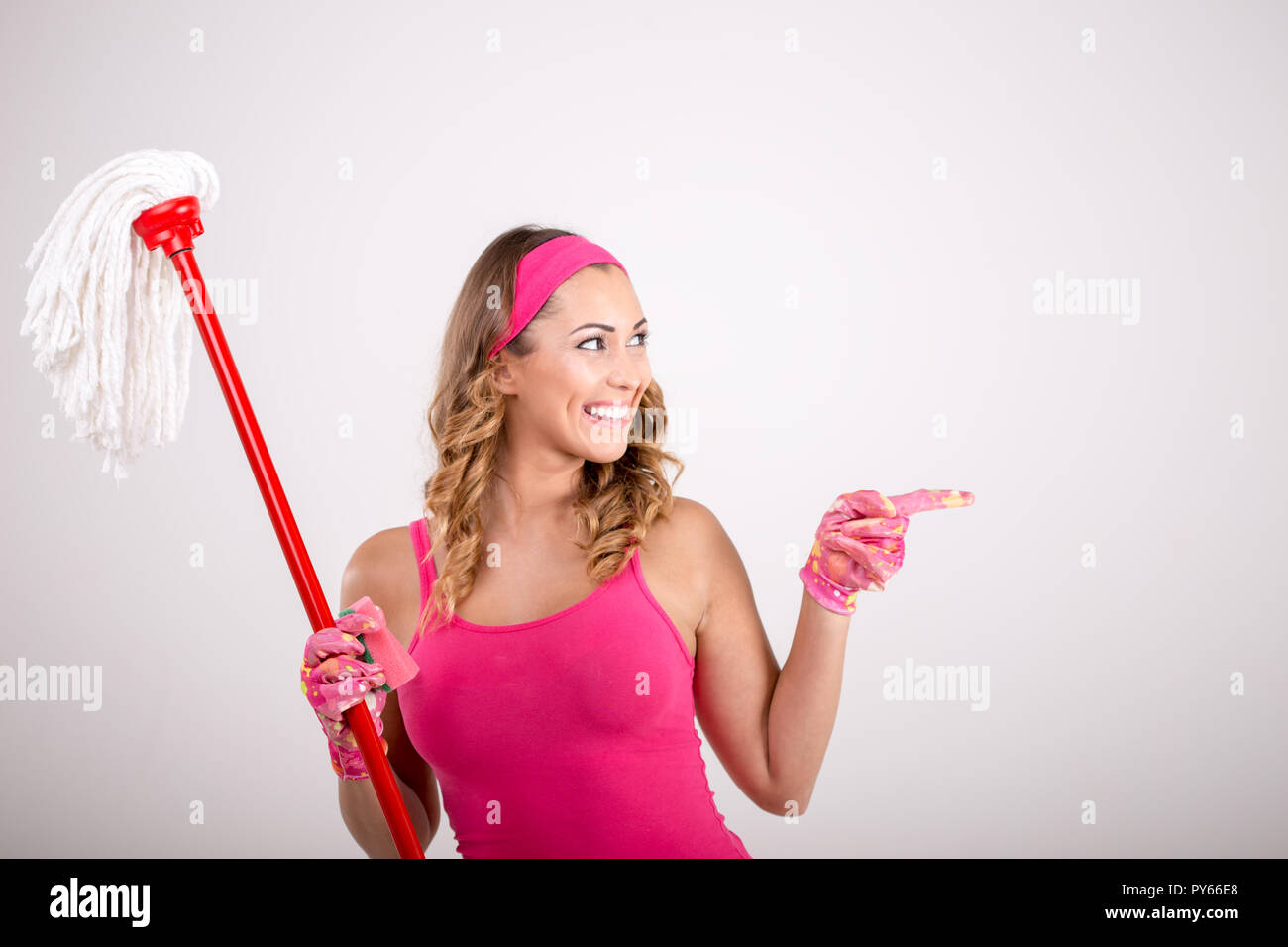 Happy woman holding a mop while pointing at something on white ...
