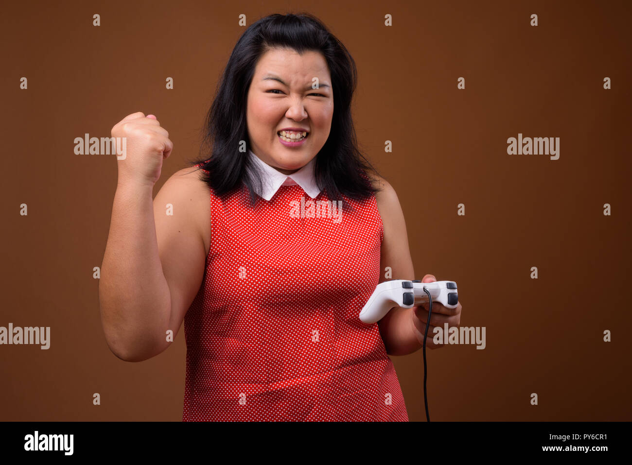 Happy overweight Asian woman playing video games using game controller ...