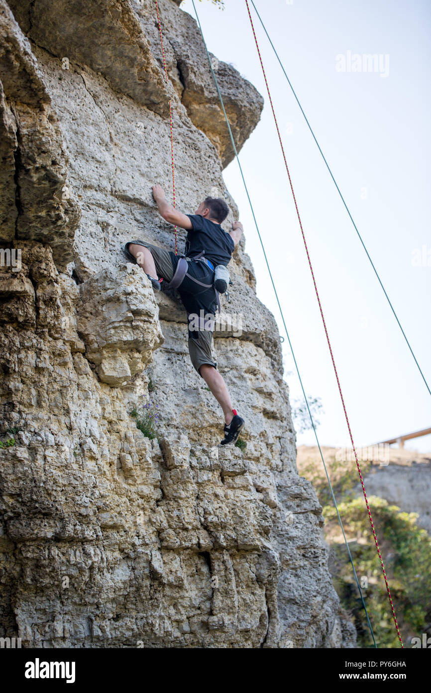 Photo of athlete man in helmet clambering over rock against background ...
