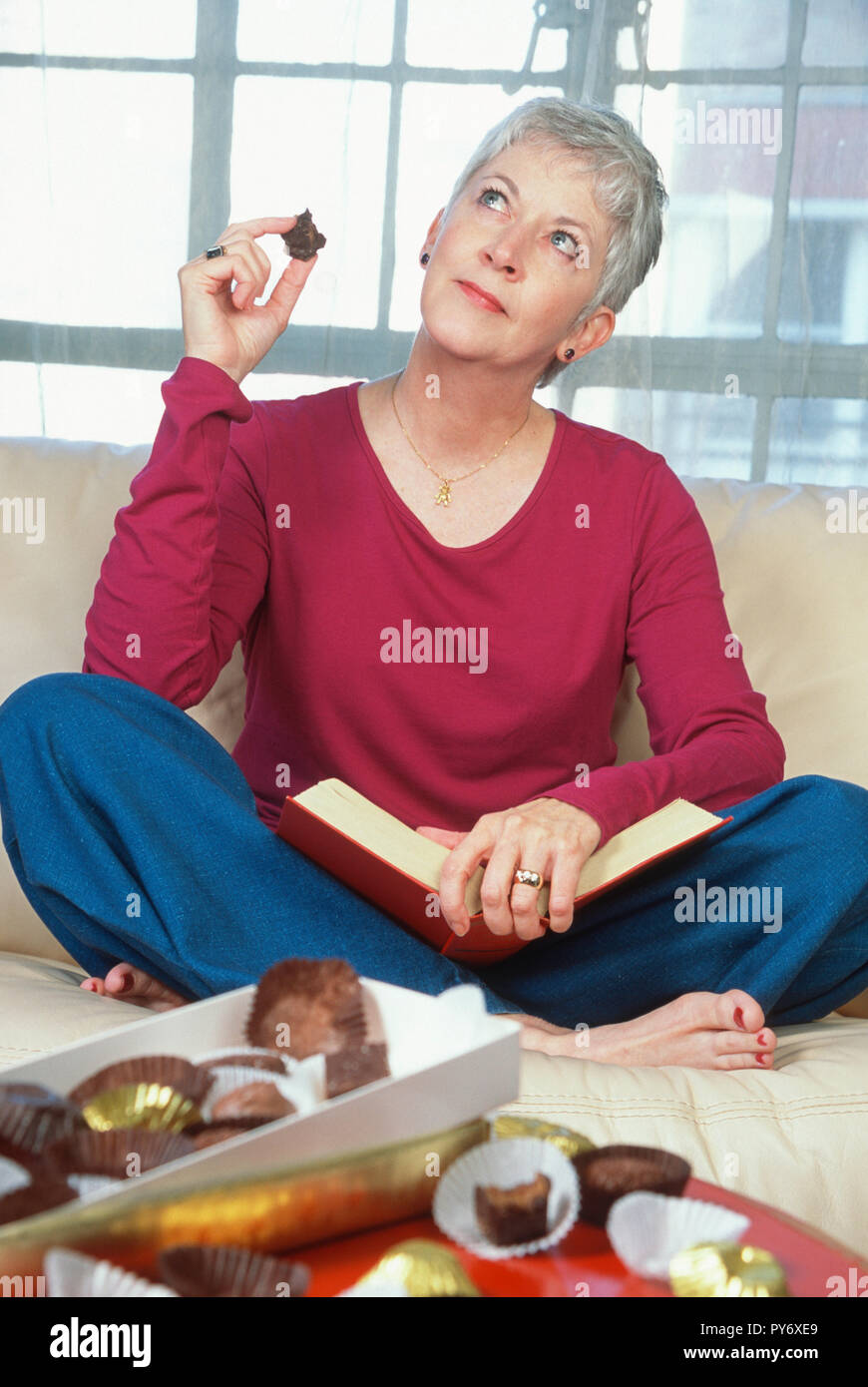 Mature woman relaxing reading a novel and eating bonbons, USA Stock ...