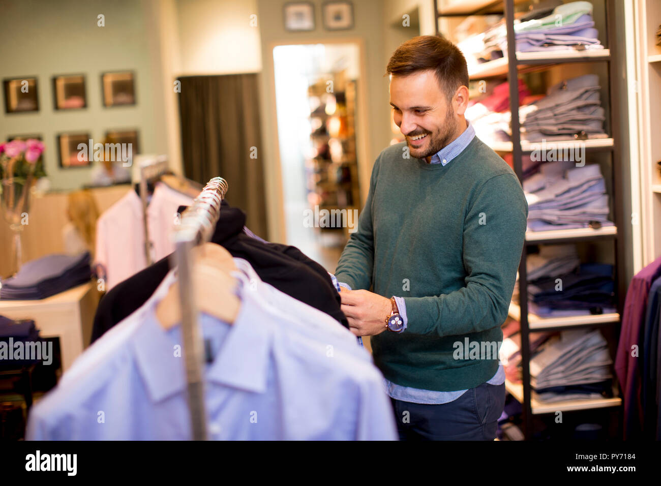 Portrait of a young cheerfull man looking at clothes to buy at shop ...