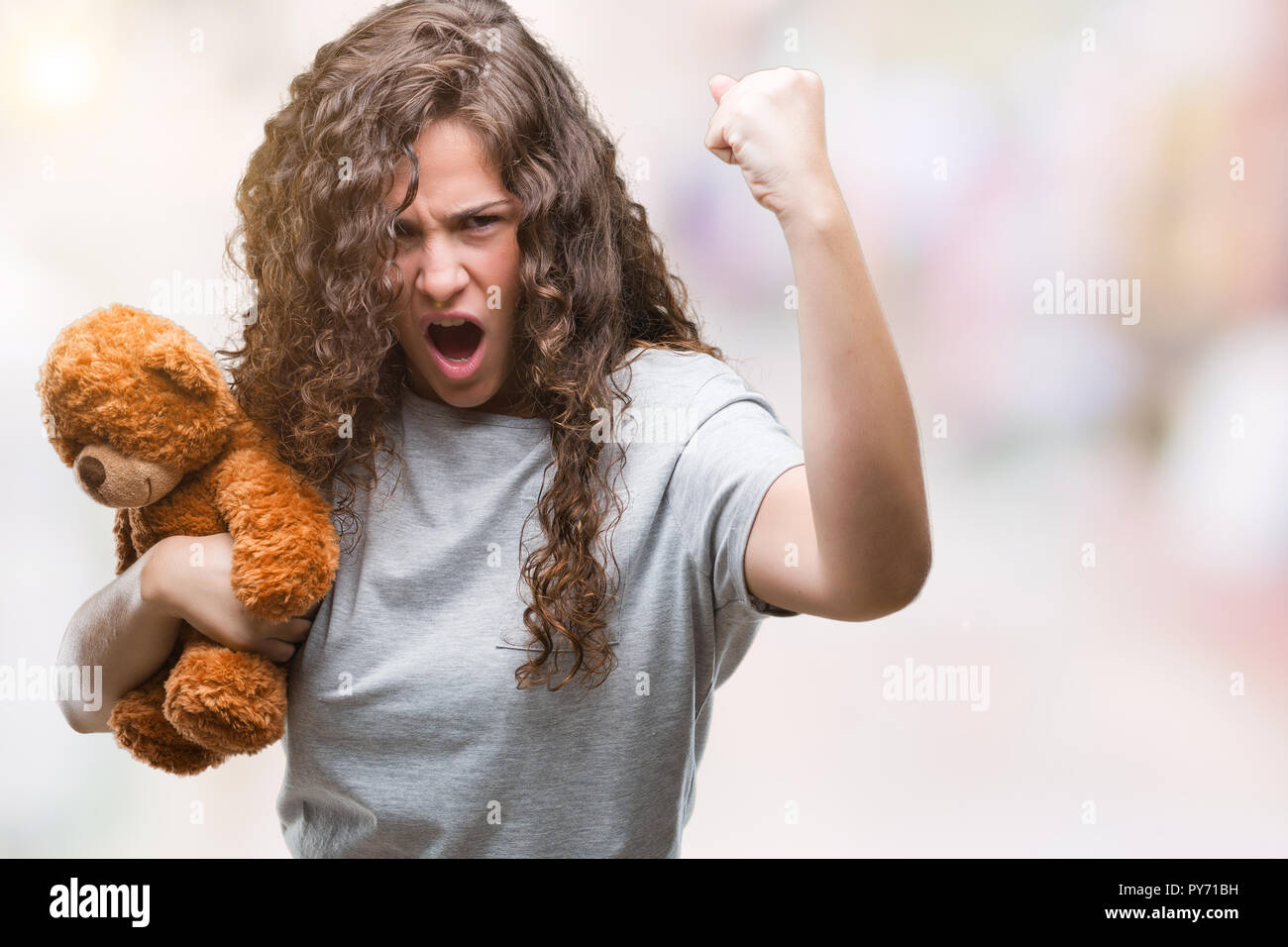 Young brunette girl holding teddy bear over isolated background annoyed ...