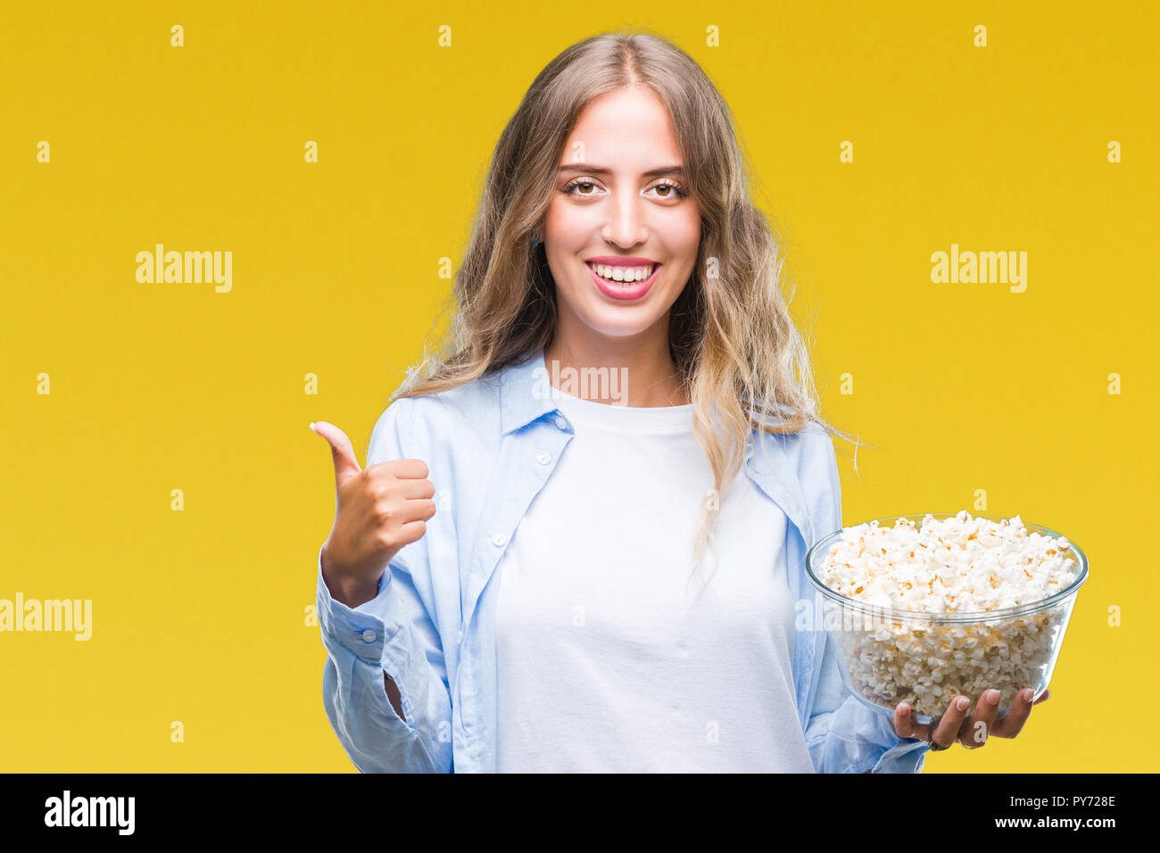 Beautiful young blonde woman eating popcorn over isolated background ...