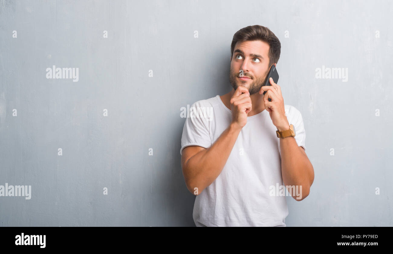 Handsome young man over grey grunge wall speaking on the phone serious ...