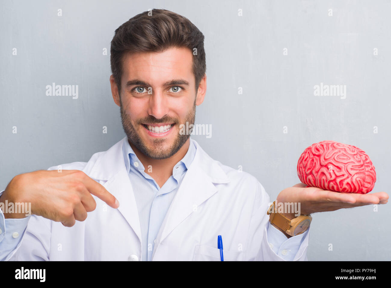 Handsome young doctor psychologist man over grey grunge wall holding a ...