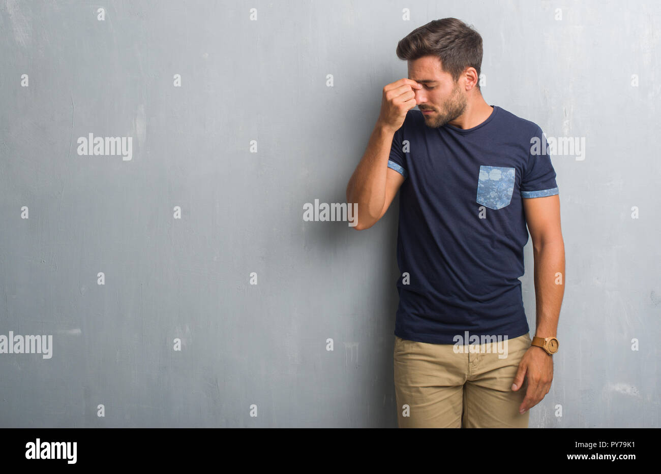 Handsome young man over grey grunge wall tired rubbing nose and eyes ...