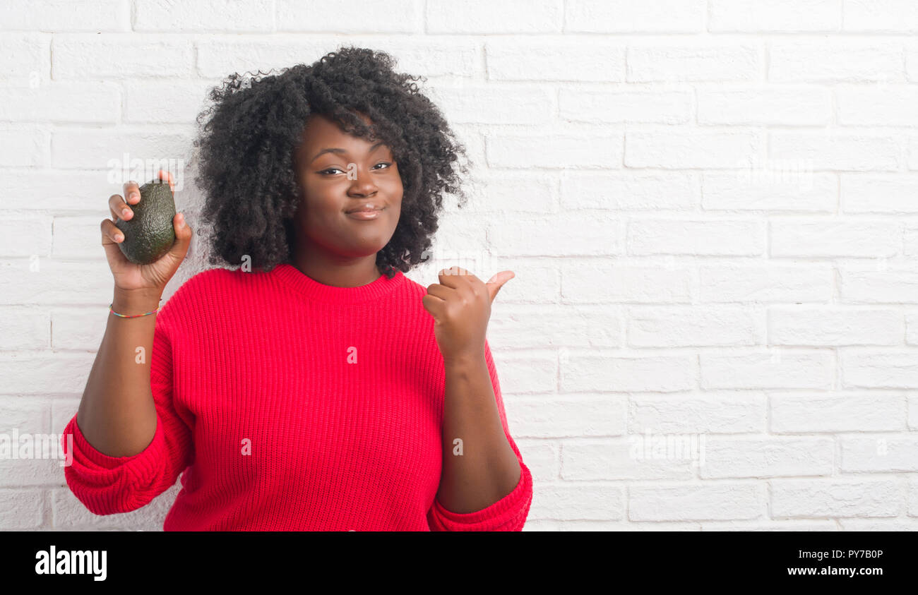 Young african american woman over white brick wall eating avocado ...
