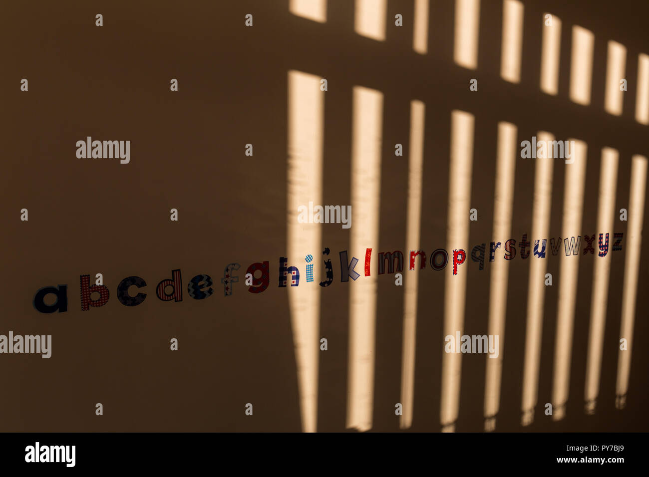 Alphabet letters on wall with light shining through blinds onto part of ...