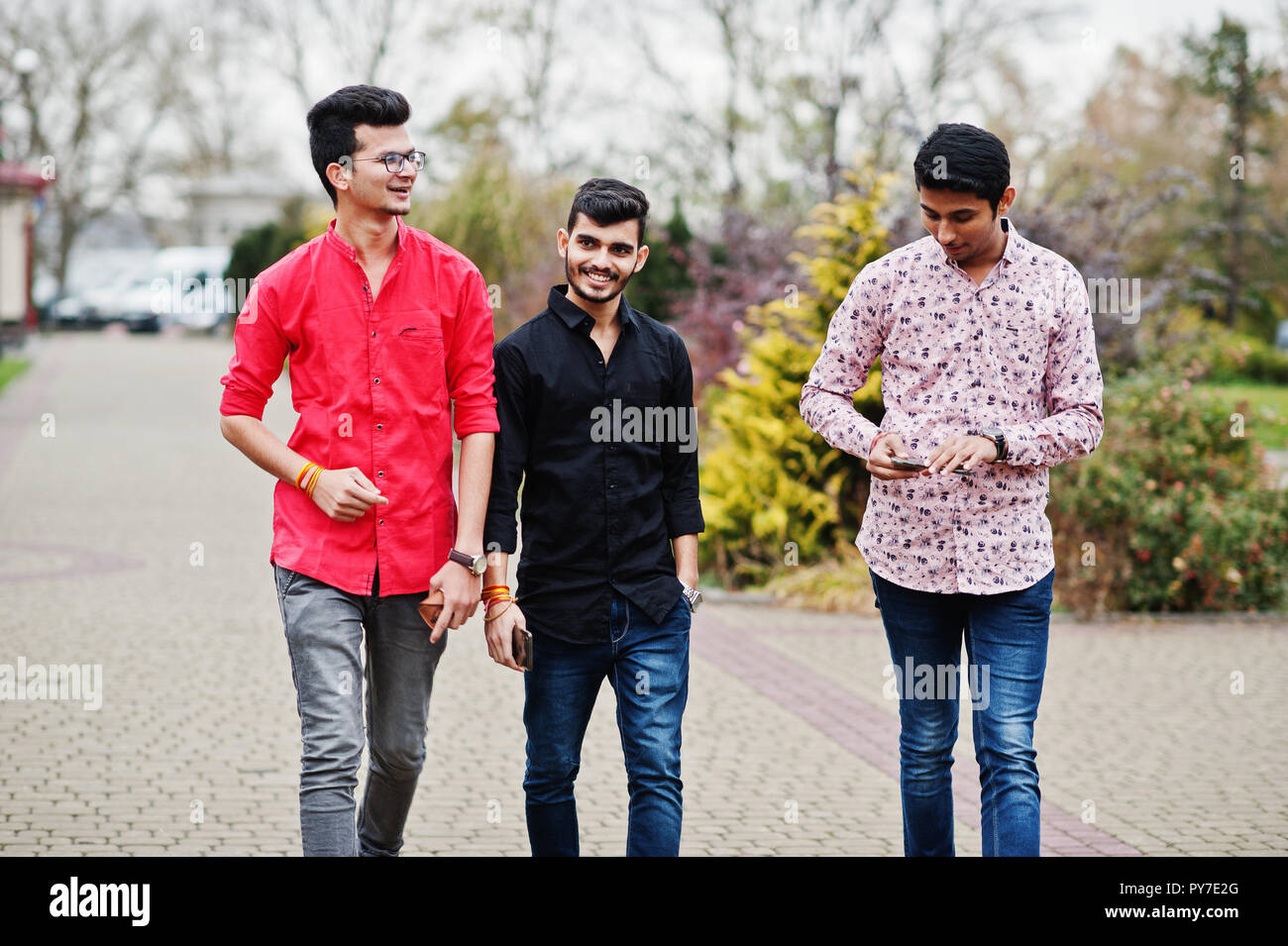 Three indian guys students friends walking on street and looking at ...