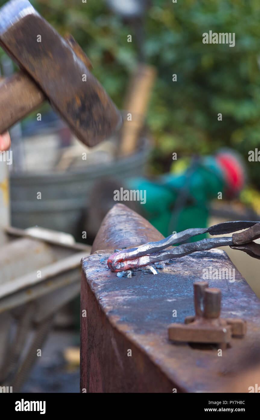 blacksmith performs the forging of hot glowing metal on the anvil ...