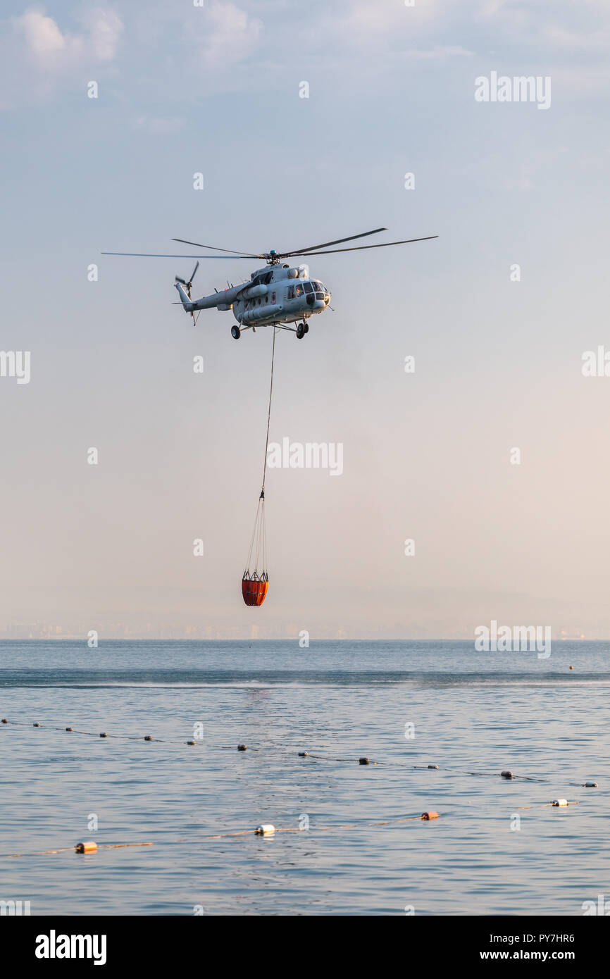A helicopter with a red basket is lowered over the sea to catch water ...