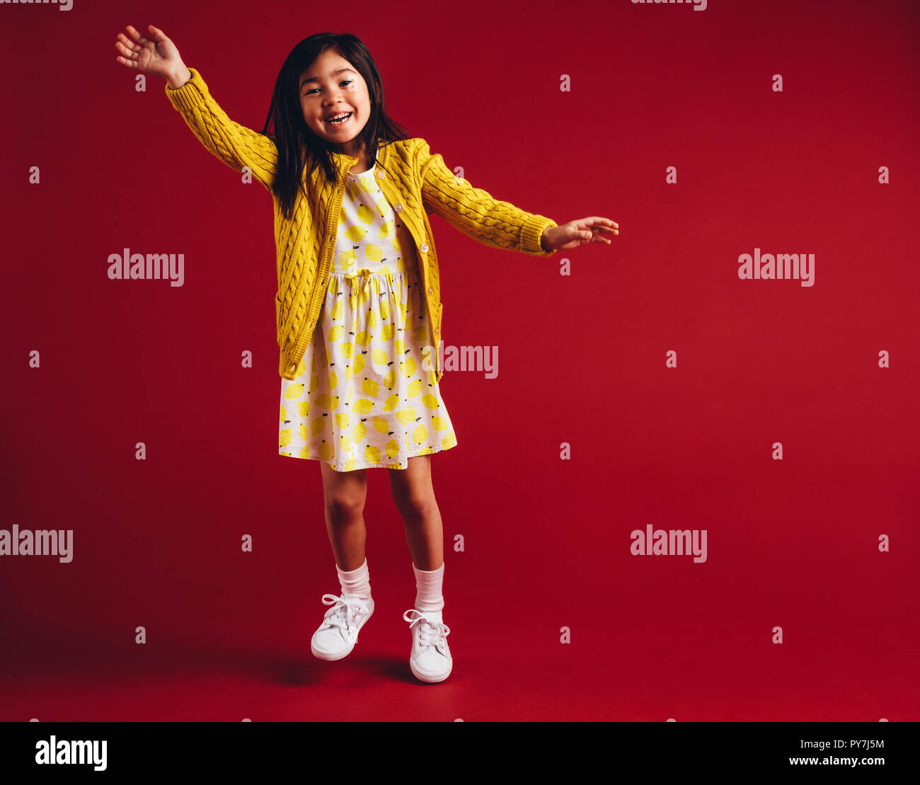 Cheerful girl waving her hand standing against a red background ...