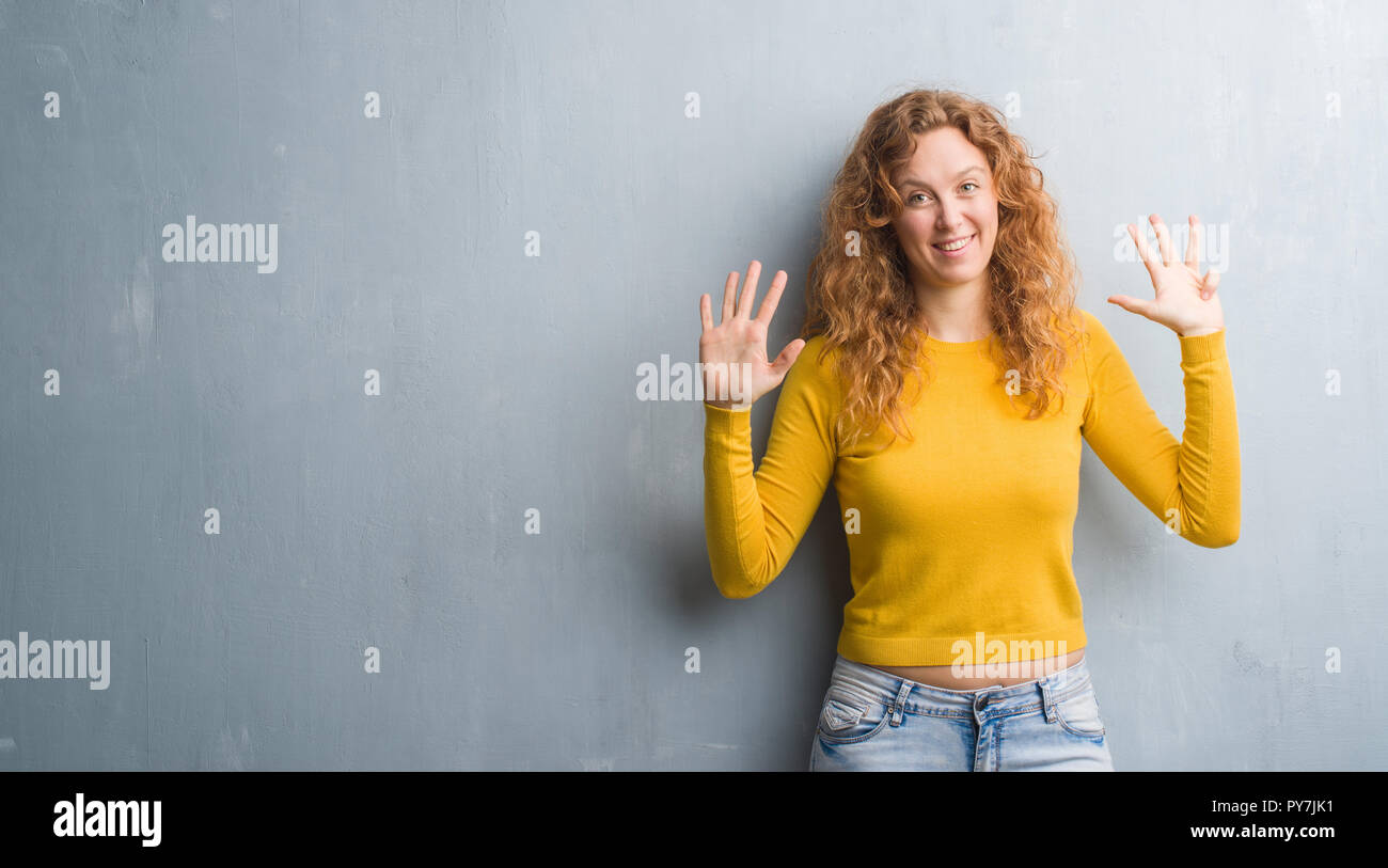 Young redhead woman over grey grunge wall showing and pointing up with ...
