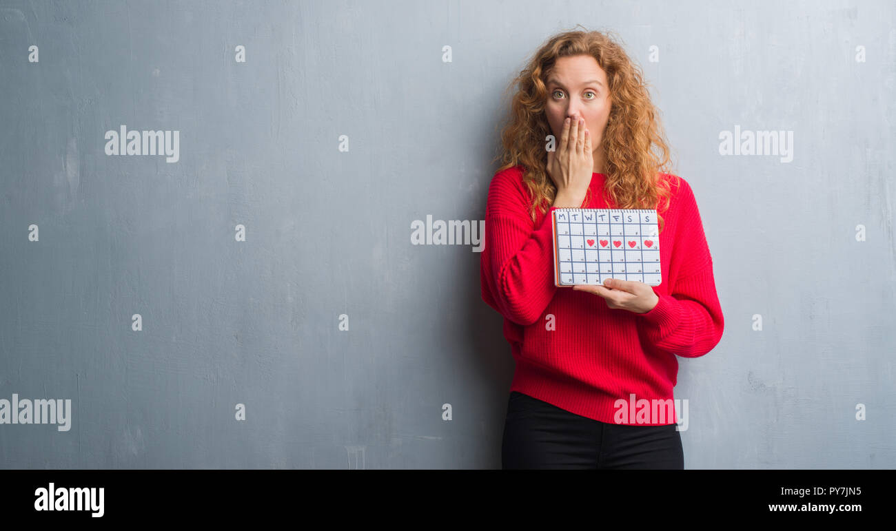 Young redhead woman over grey grunge wall holding period calendar cover ...