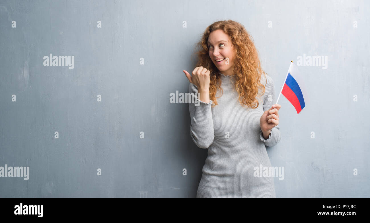 Young redhead woman over grey grunge wall holding flag of Russia ...
