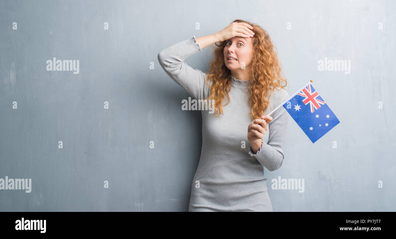 Young redhead woman over grey grunge wall holding flag of Australia ...