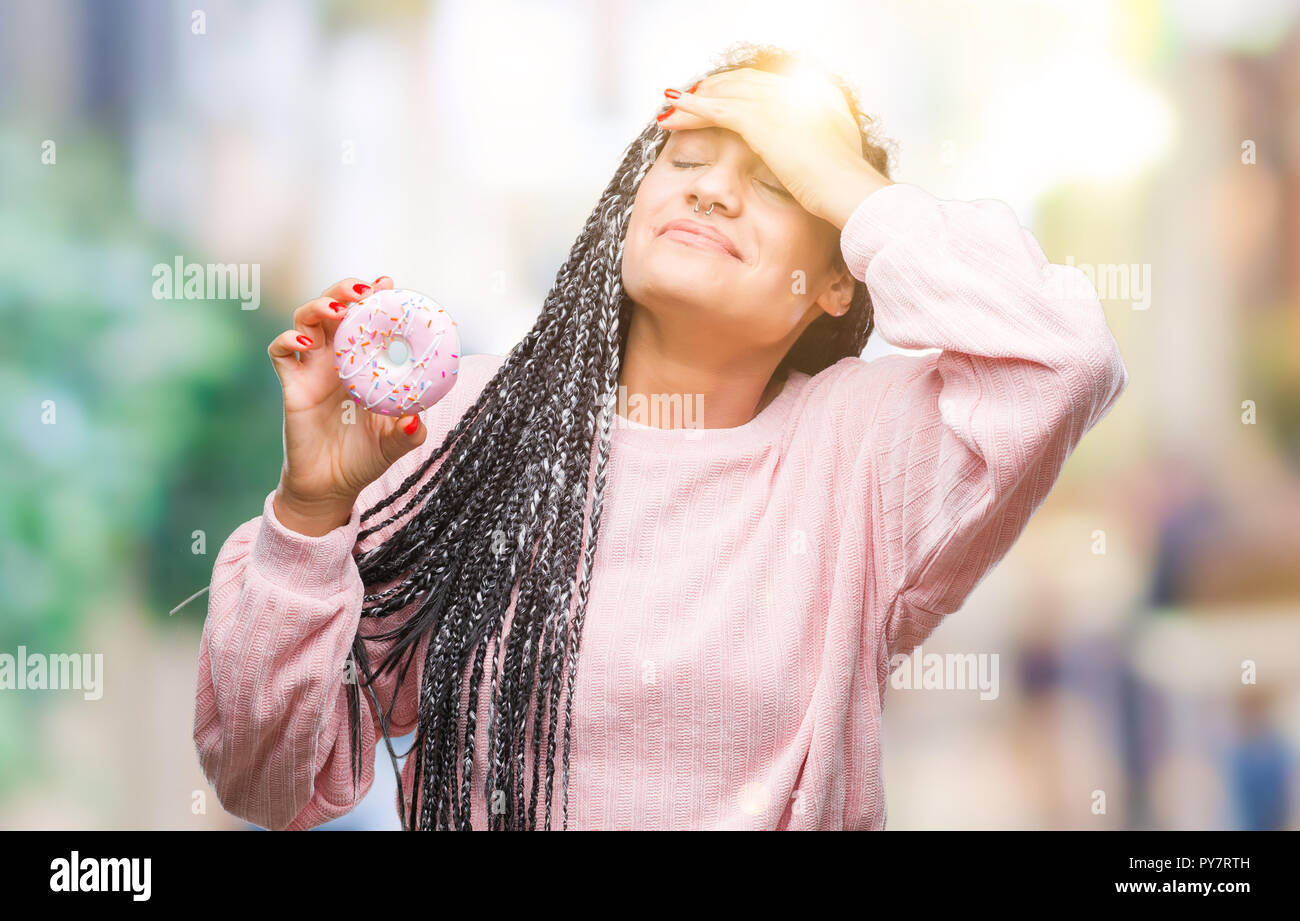 Young african american girl eating pink donut over isolated background ...