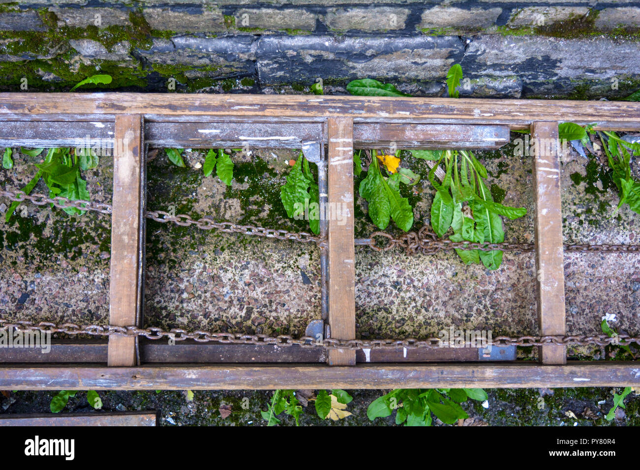 An old wooden ladder stepladder with rusty large chains lies on a ...