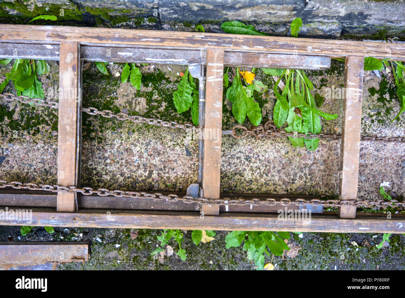An old wooden ladder stepladder with rusty large chains lies on a ...