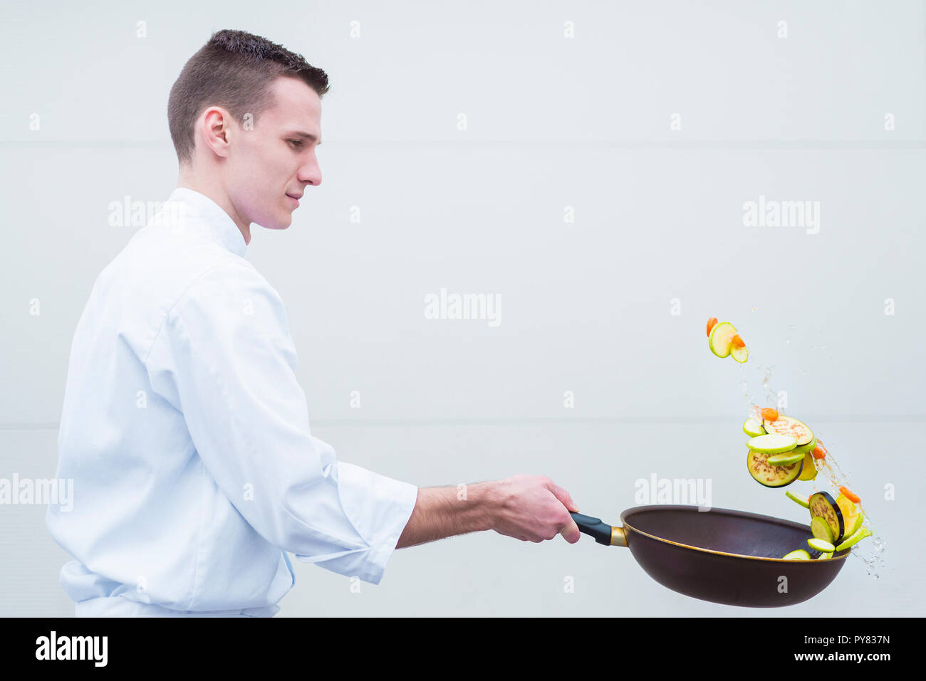 Young chef flipping vegetables in frying pan side view Stock Photo - Alamy