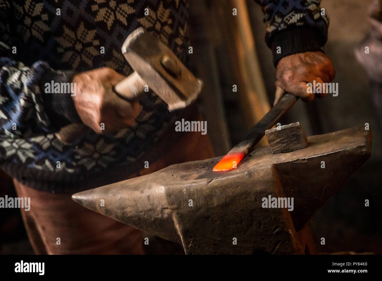 Old blacksmith manually forging molten metal with hammer on the anvil ...