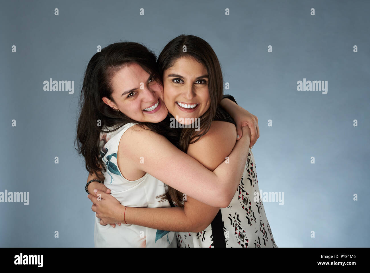 Two young smiling girl friends hugging on studio background Stock Photo ...
