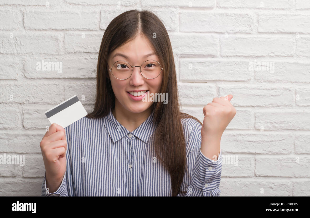 Young Chinese woman over brick wall holding credit card screaming proud ...