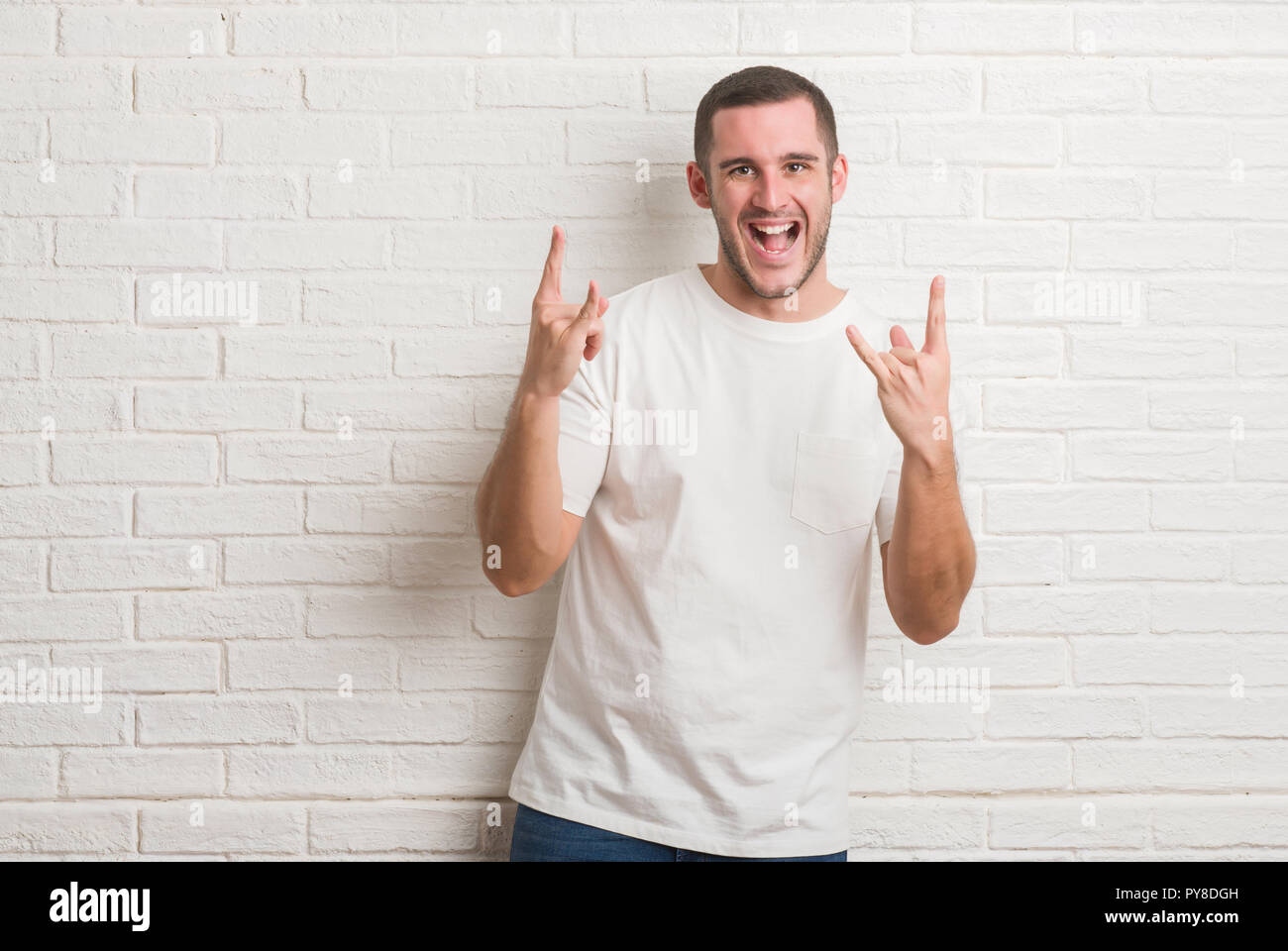 Young caucasian man standing over white brick wall covering eyes with ...