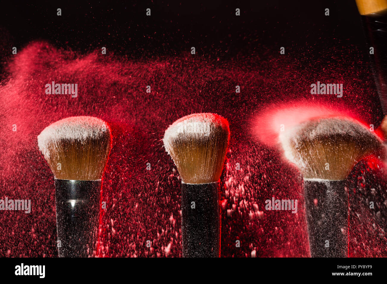 Mineral makeup and cosmetics concept - Three makeup brushes in red dust ...