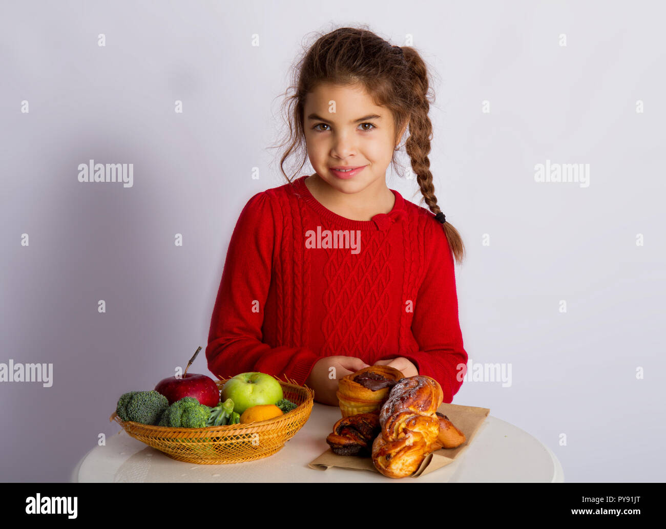 Little girl chooses what to eat, healthy food or buns Stock Photo - Alamy