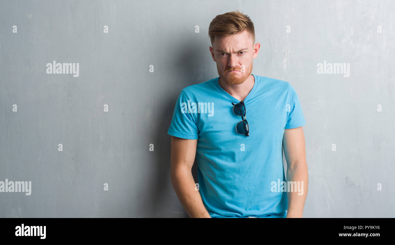 Young redhead man over grey grunge wall wearing casual outfit depressed ...