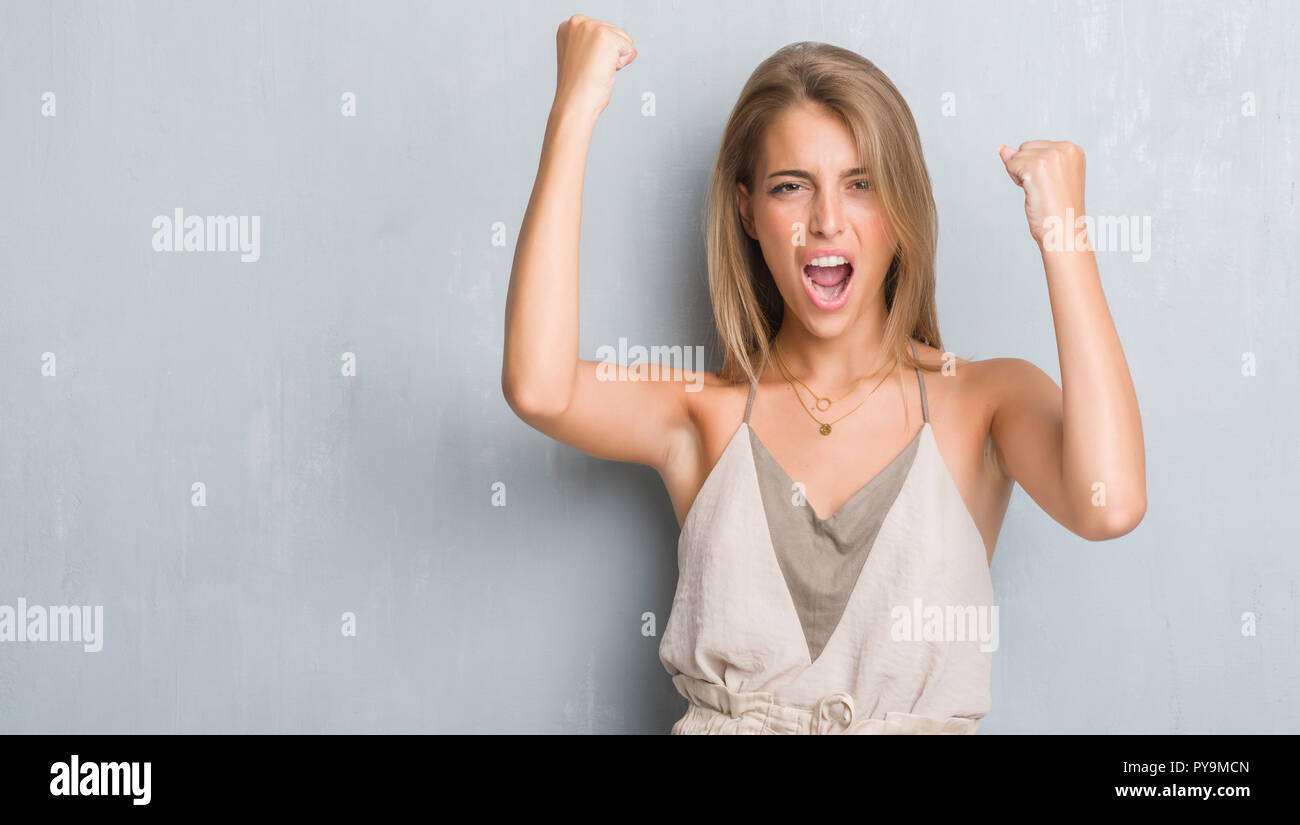 Beautiful young woman standing over grunge grey wall annoyed and ...