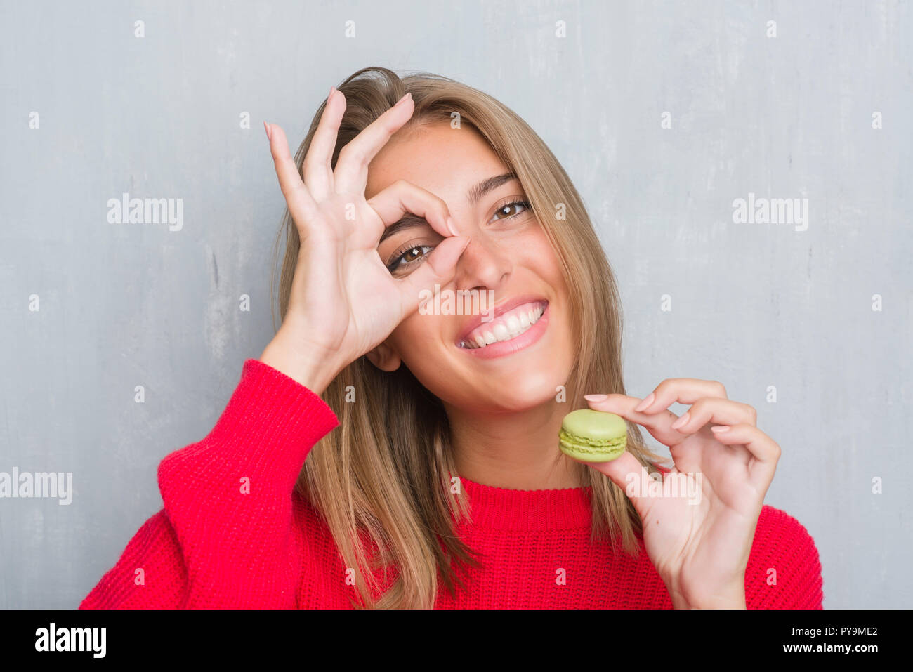 Beautiful young woman over grunge grey wall eating green macaron with ...