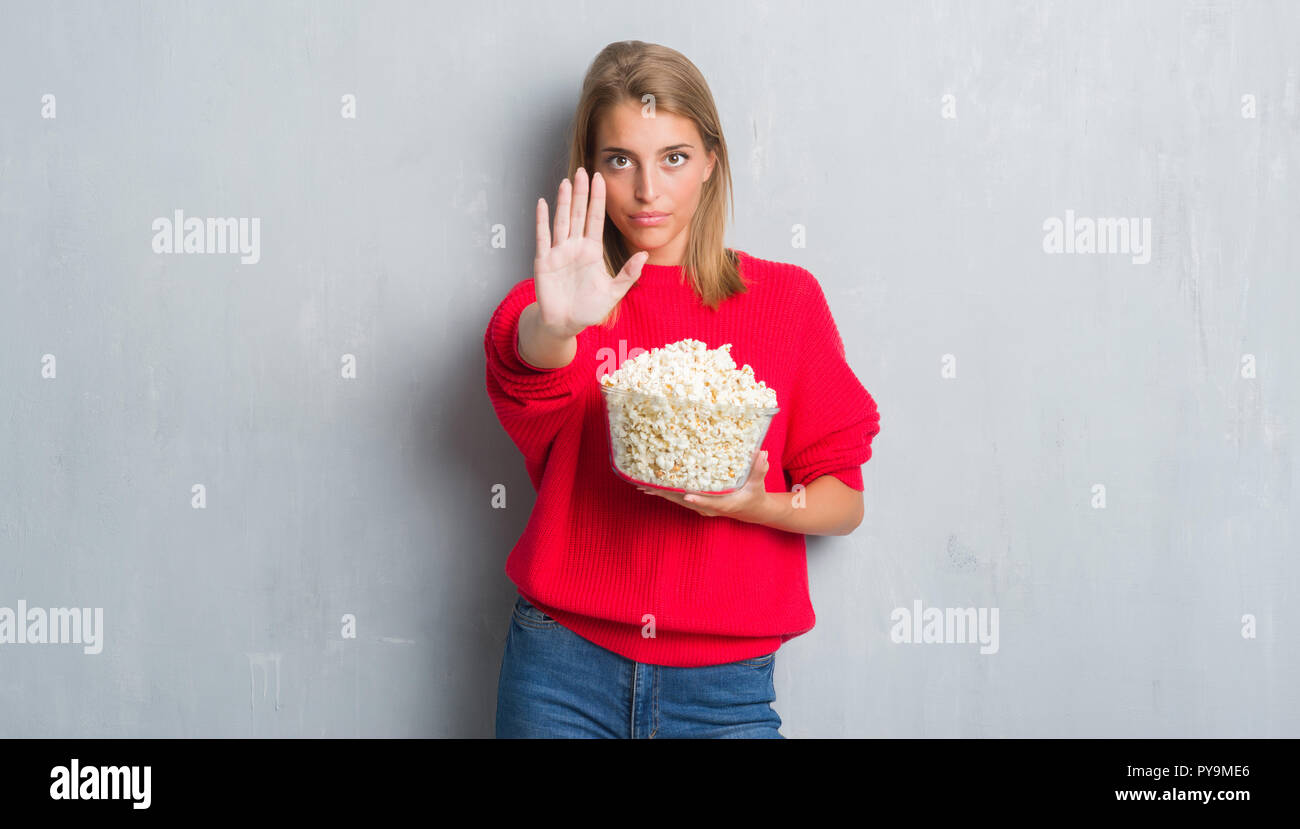 Beautiful young woman over grunge grey wall eating pop corn with open ...