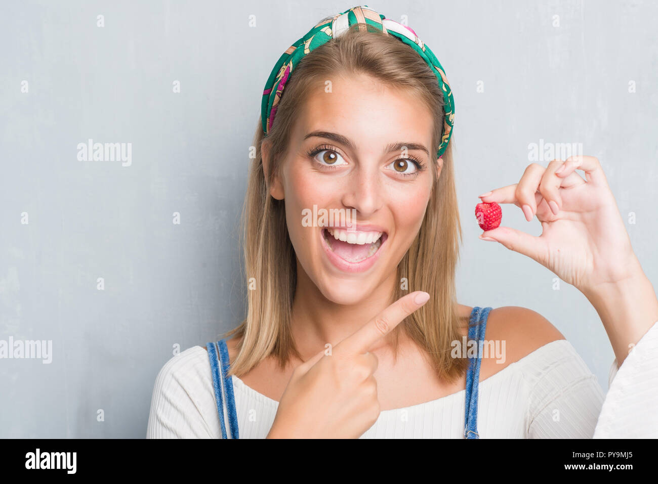 Beautiful young woman over grunge grey wall eating fresh raspberry very ...