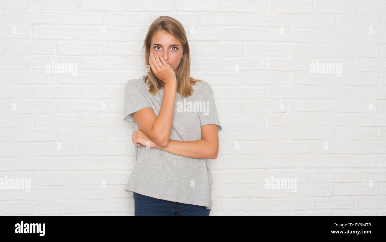 Beautiful young woman over white brick wall thinking looking tired and ...