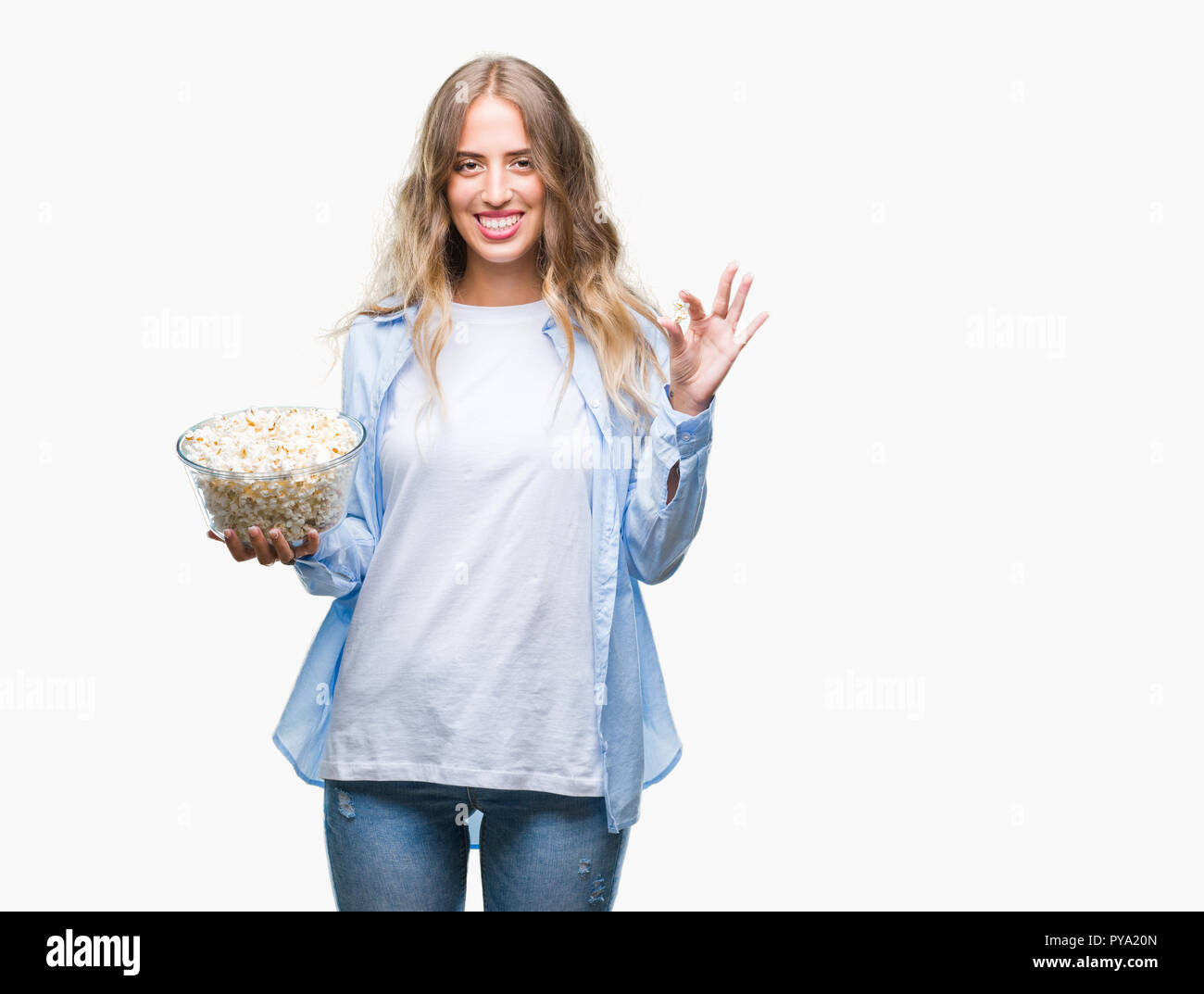 Beautiful young blonde woman eating popcorn over isolated background ...