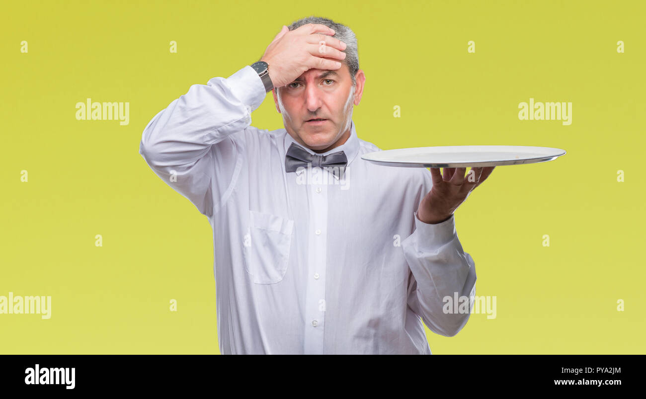 Handsome senior waiter man holding silver tray over isolated background ...