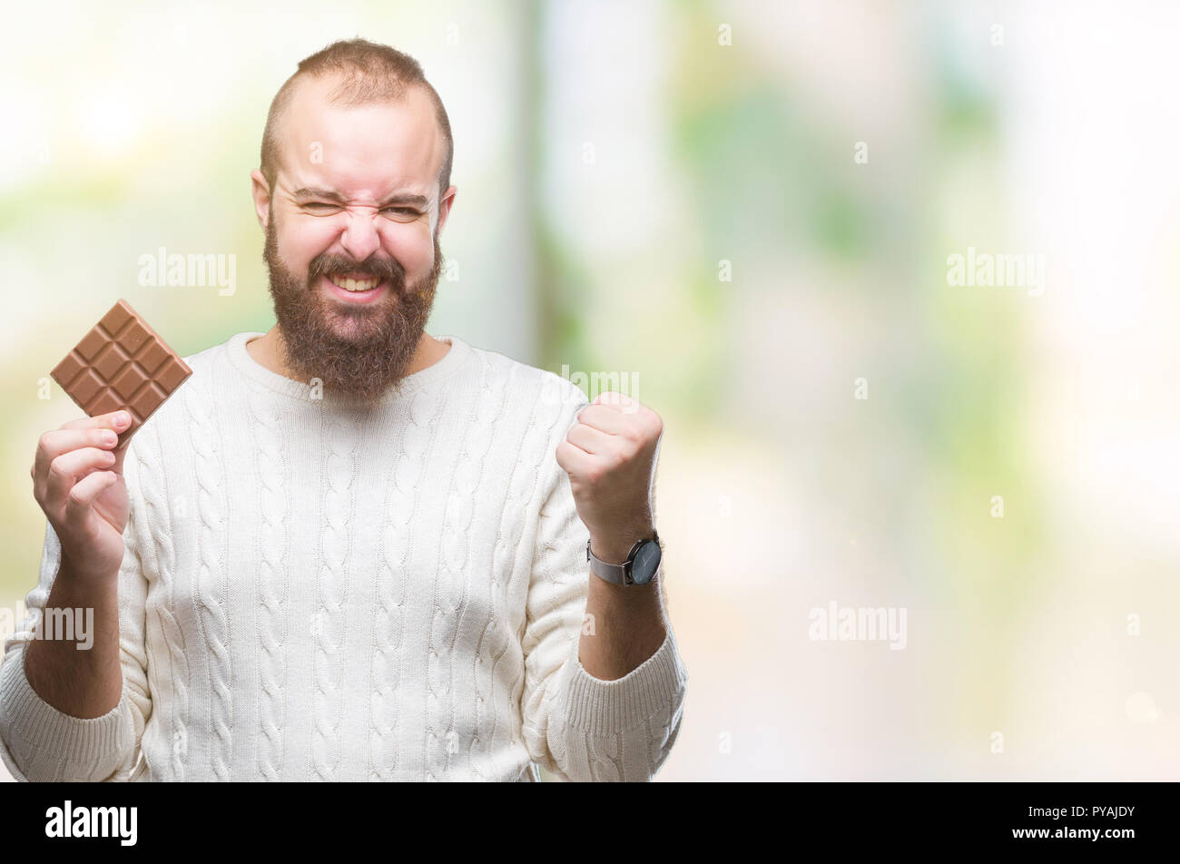 Young hipster man eating chocolate bar over isolated background ...