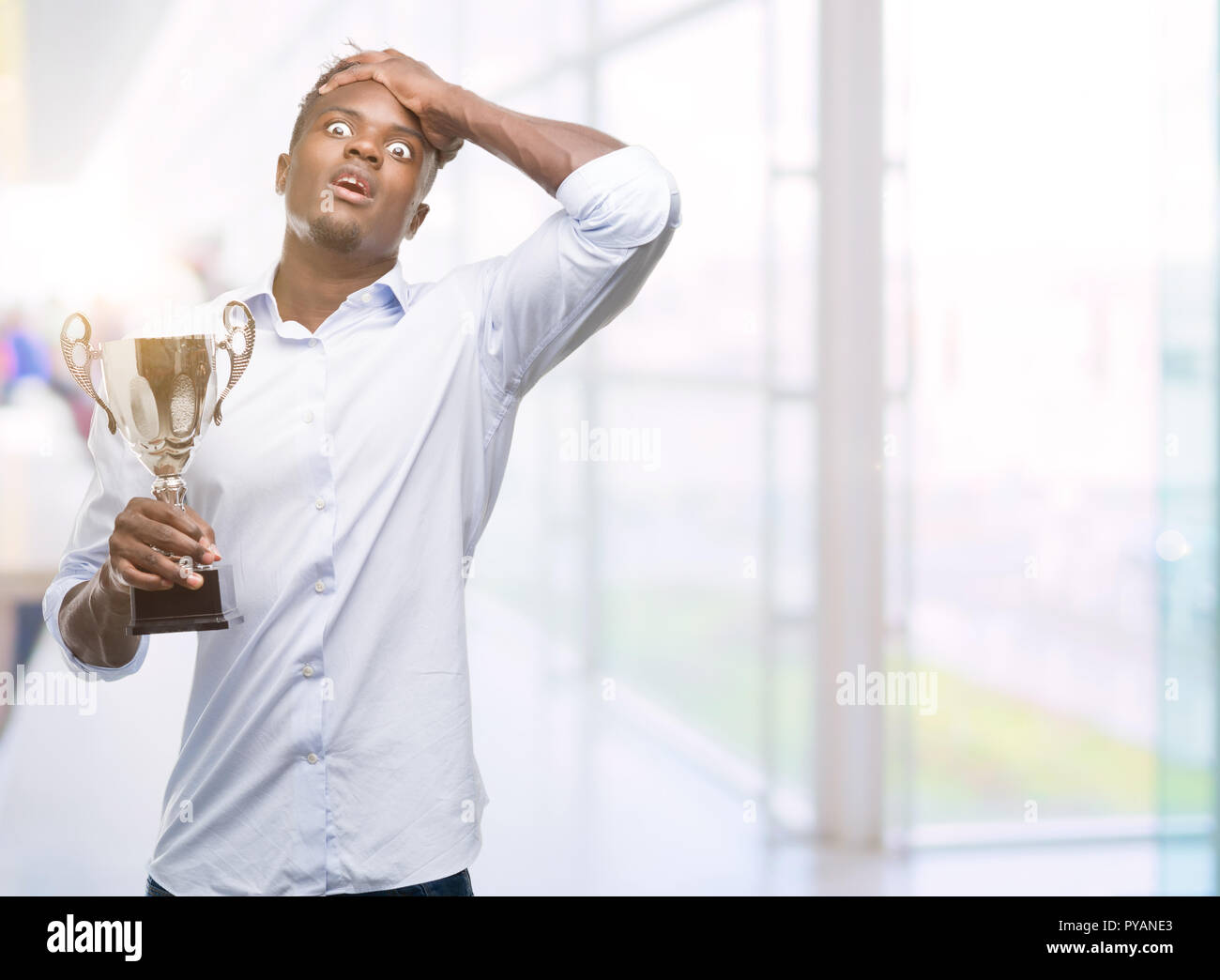 Young african american man holding trophy stressed with hand on head ...