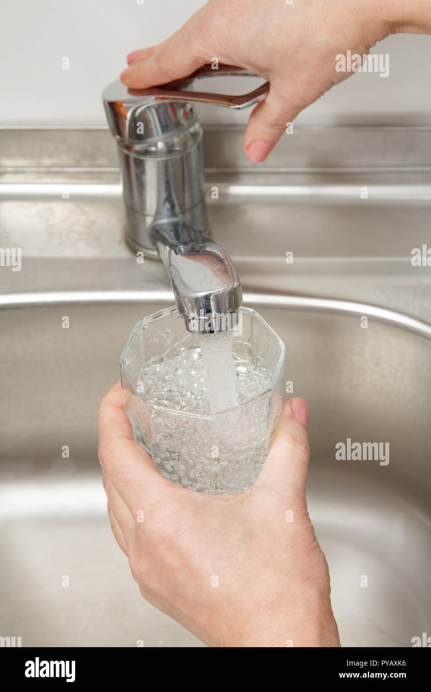 Glass in female hand is filled with clean transparent water under the ...