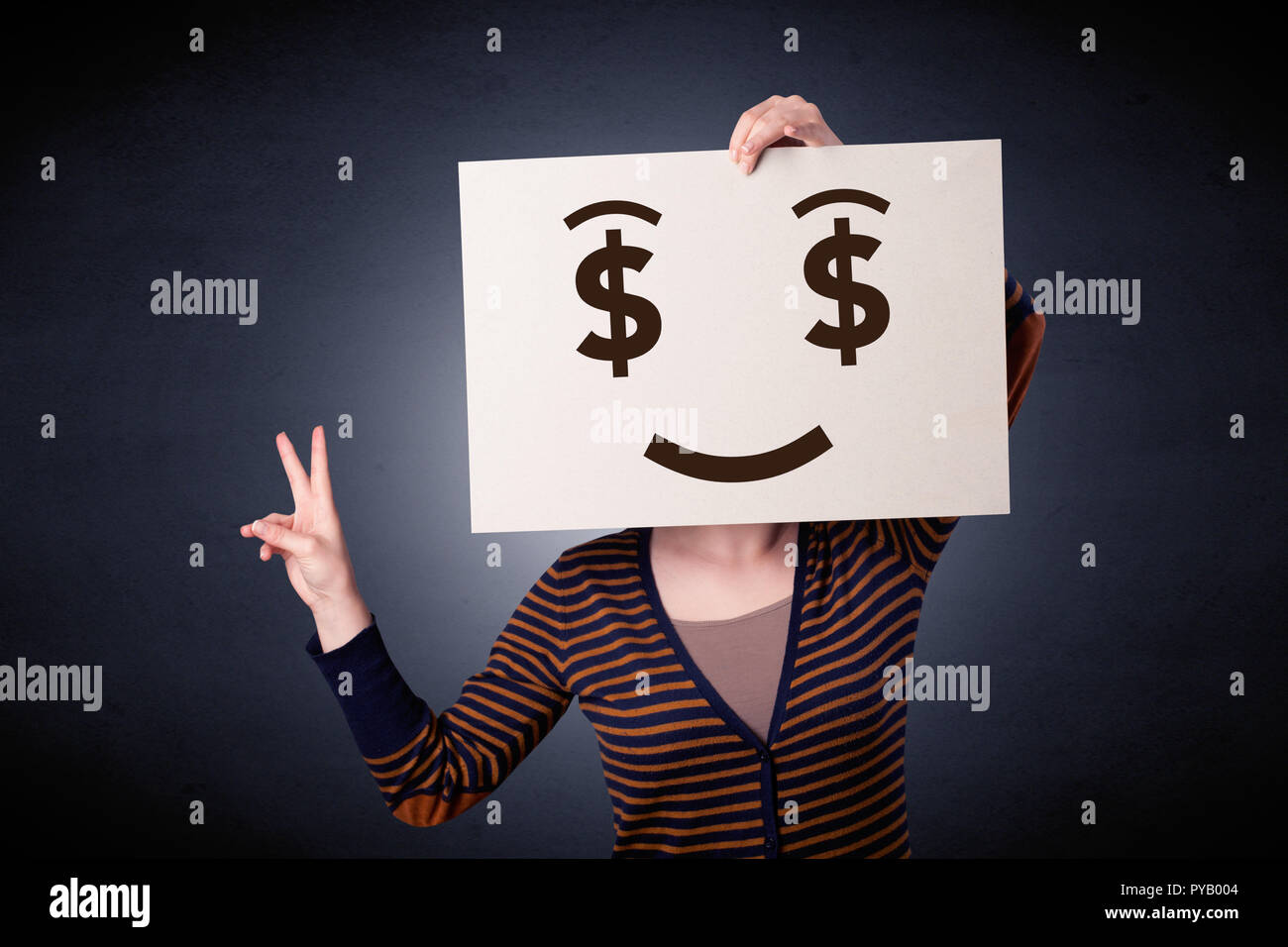 Young casual woman hiding behind a greedy face drawing on cardboard ...