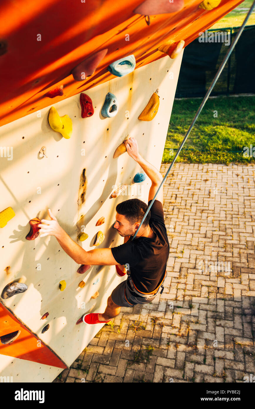 Man wearing belaying rope, climbing on a very high rock climbing wall ...