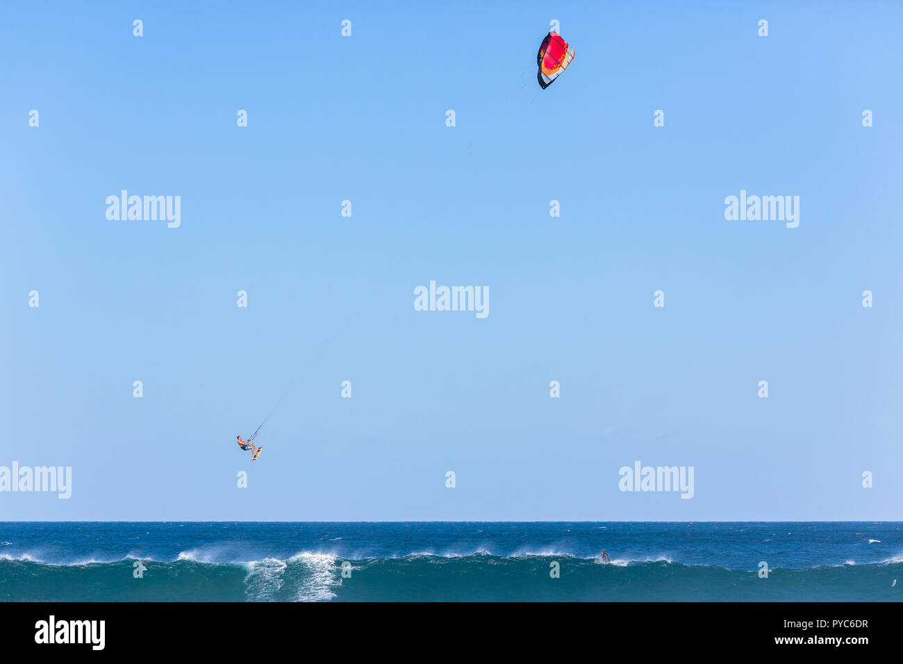Kite surfer surfing wind flying ocean wave launch high into blue sky ...