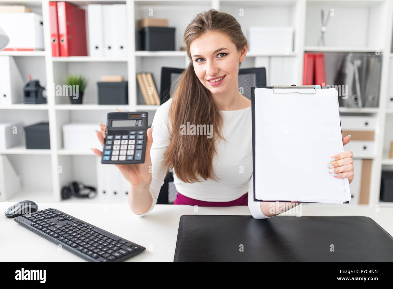 A young girl sitting at a table and holding a calculator and a blank ...